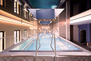 Piscina interior moderna com barreira de vidro, teto estrelado e vista para a área da piscina.