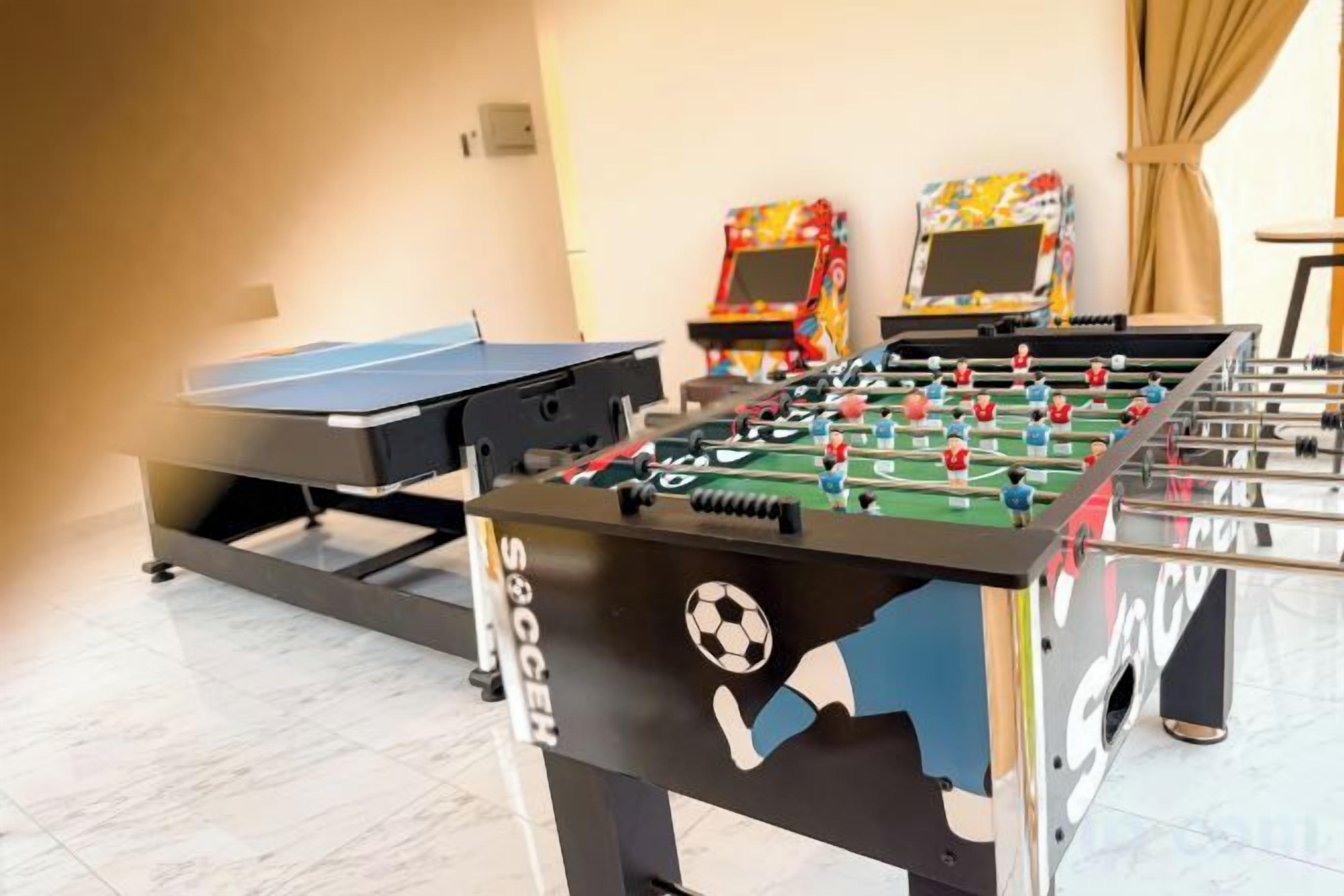Uma mesa de futebol de mesa e duas máquinas de jogos de arcade em um ambiente com piso ladrilhado.