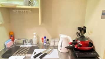 Uma cozinha com pia, tábua de corte, chaleira, panela vermelha e vários frascos.