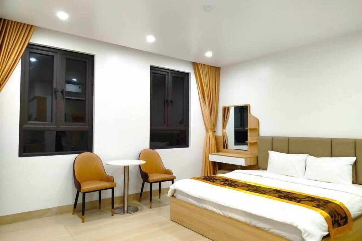 Quarto de hotel com uma cama, duas cadeiras, uma mesinha e um espelho.