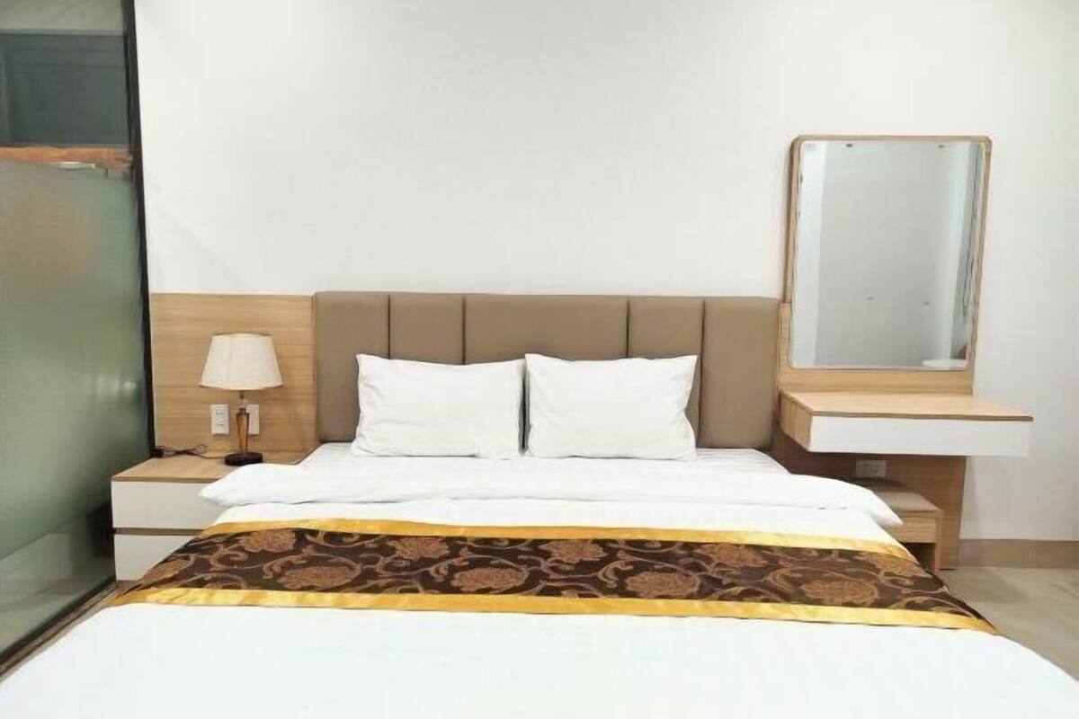 Quarto de hotel com cama, mesa de cabeceira, abajur e espelho.