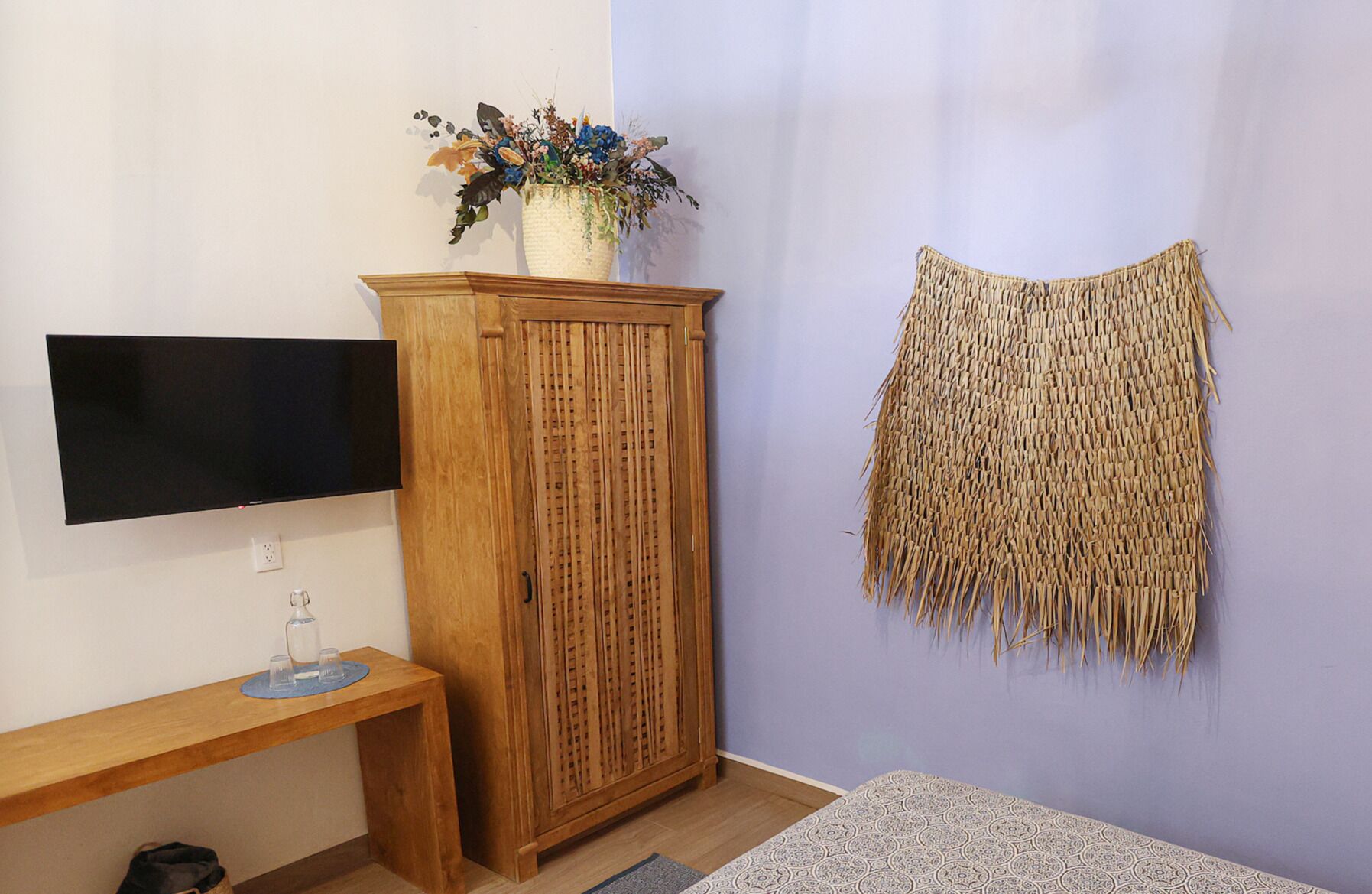 Quarto com armário de madeira, televisão de tela plana, mesinha com um copo e um objeto pendurado na parede.