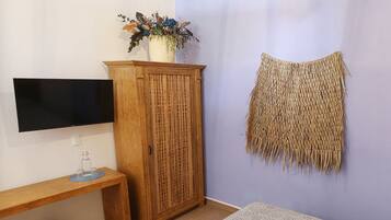 Quarto com armário de madeira, televisão de tela plana, mesinha com um copo e um objeto pendurado na parede.