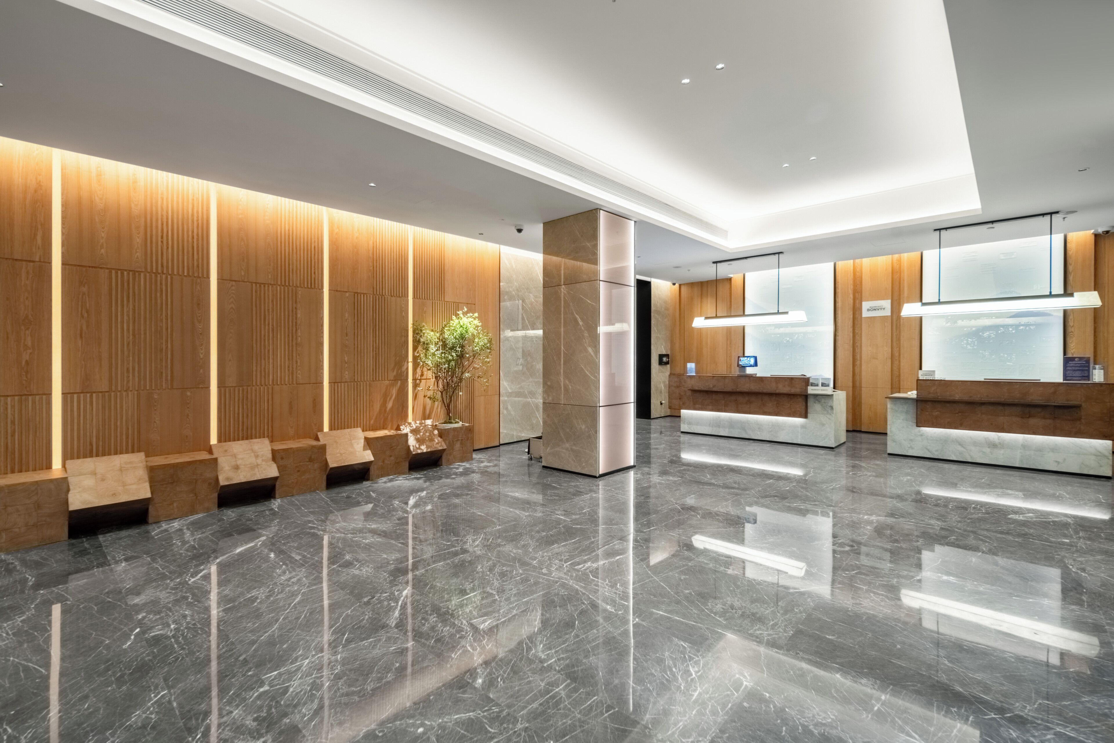 Uma área de recepção moderna com piso de mármore, painéis de madeira e um balcão de atendimento.