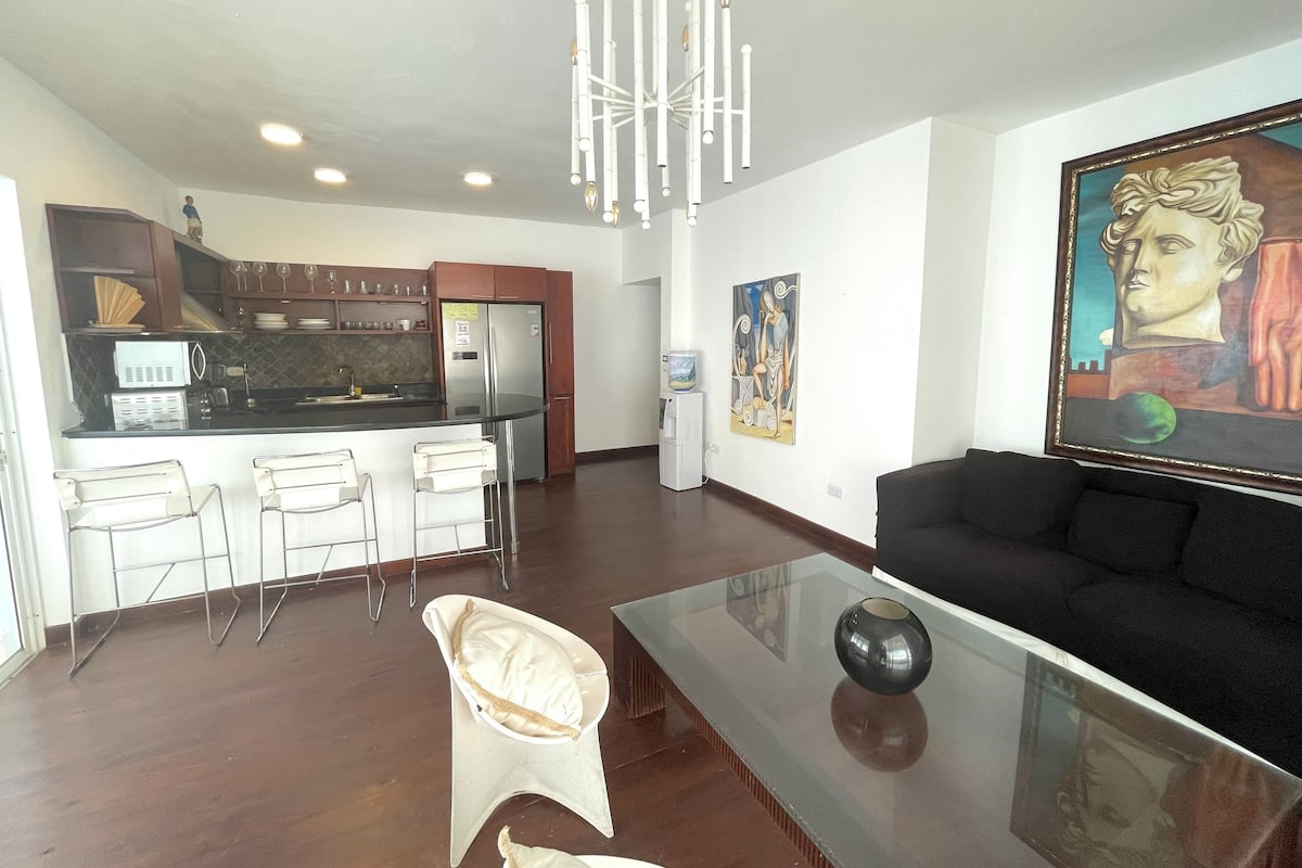 Uma sala de estar moderna com uma mesa de centro de vidro, um sofá preto e uma pintura na parede.