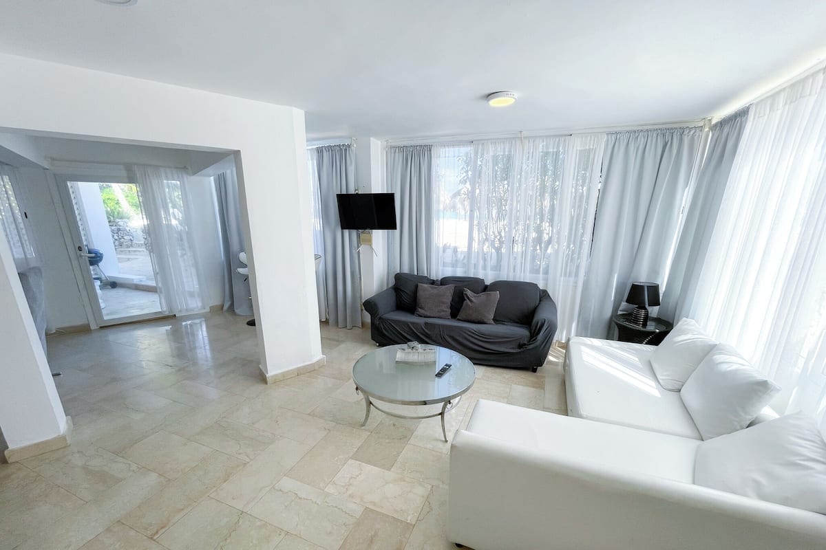 Uma sala de estar moderna com um sofá cinzento, um sofá branco, uma mesa de centro de vidro e uma televisão de tela plana fixada na parede.