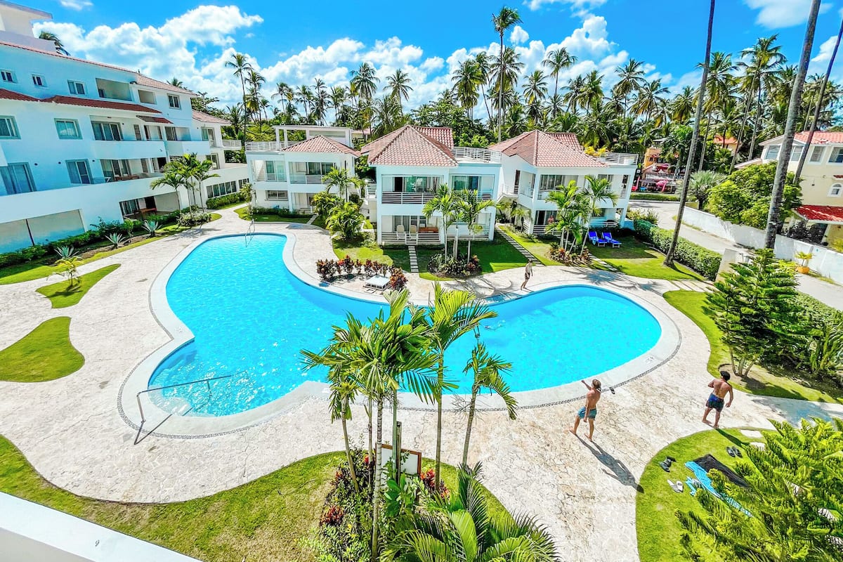 Um resort com uma piscina grande, vários edifícios e palmeiras.