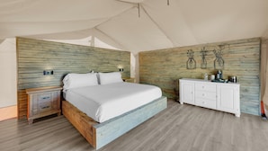 Quarto com cama de madeira, roupa de cama branca, mesa de cabeceira, penteadeira e parede com design em painel de madeira.