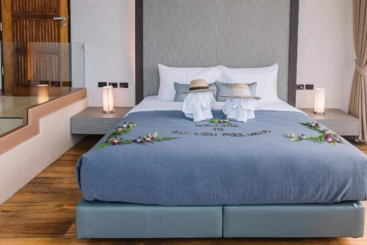Quarto moderno com uma cama grande, duas mesas de cabeceira, uma porta de madeira e vista para uma piscina.