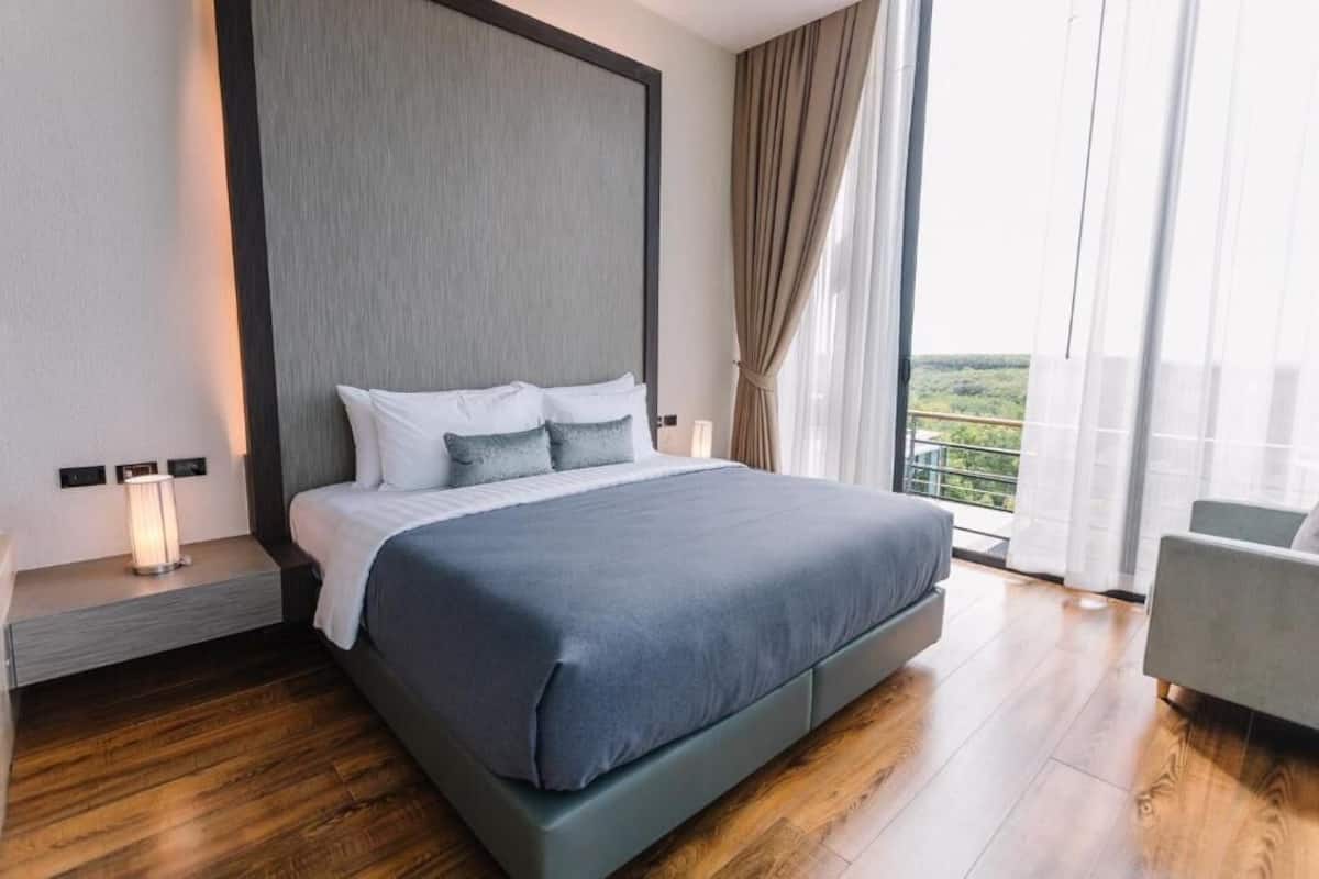 Quarto de hotel moderno com uma cama grande, mesa de cabeceira, luminária e vista para o exterior.