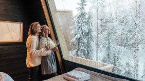 Um casal em pé perto de uma janela com vista para árvores cobertas de neve.