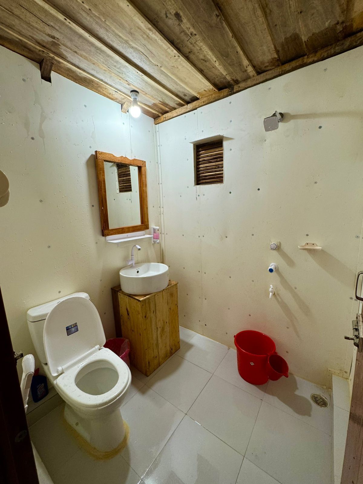 Uma casa de banho pequena e simples, com sanita, lavatório e chuveiro.