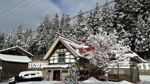 Uma cabana de madeira tradicional com telhado inclinado, rodeada por árvores cobertas de neve.
