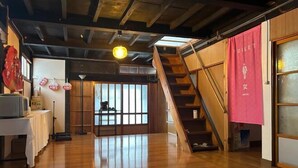 Um interior japonês tradicional com soalho de madeira, escadaria e vista através de um ecrã shoji.