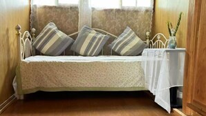 Uma cama de solteiro com colcha florida, almofadas listradas e uma pequena mesa com um vaso.