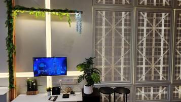 Quarto moderno com escrivaninha, televisão e planta decorativa.