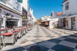 Rua de pedra com mesas ao ar livre e edifícios em ambos os lados.