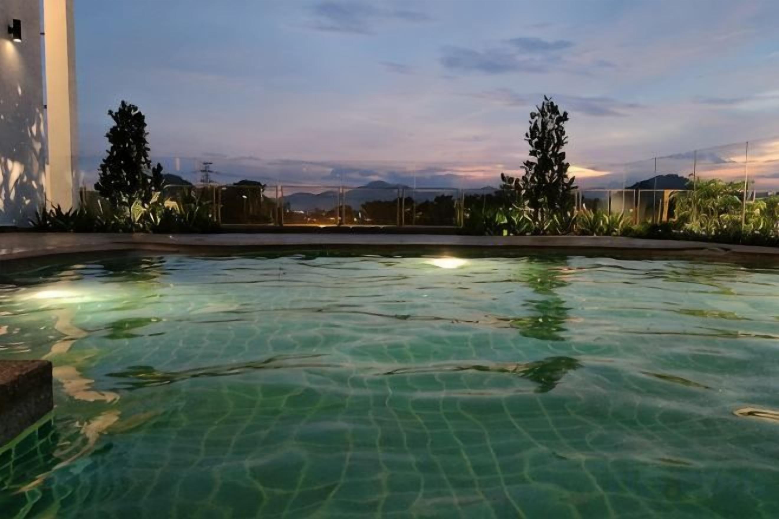 Piscina com água cristalina, rodeada por vegetação e um edifício branco.