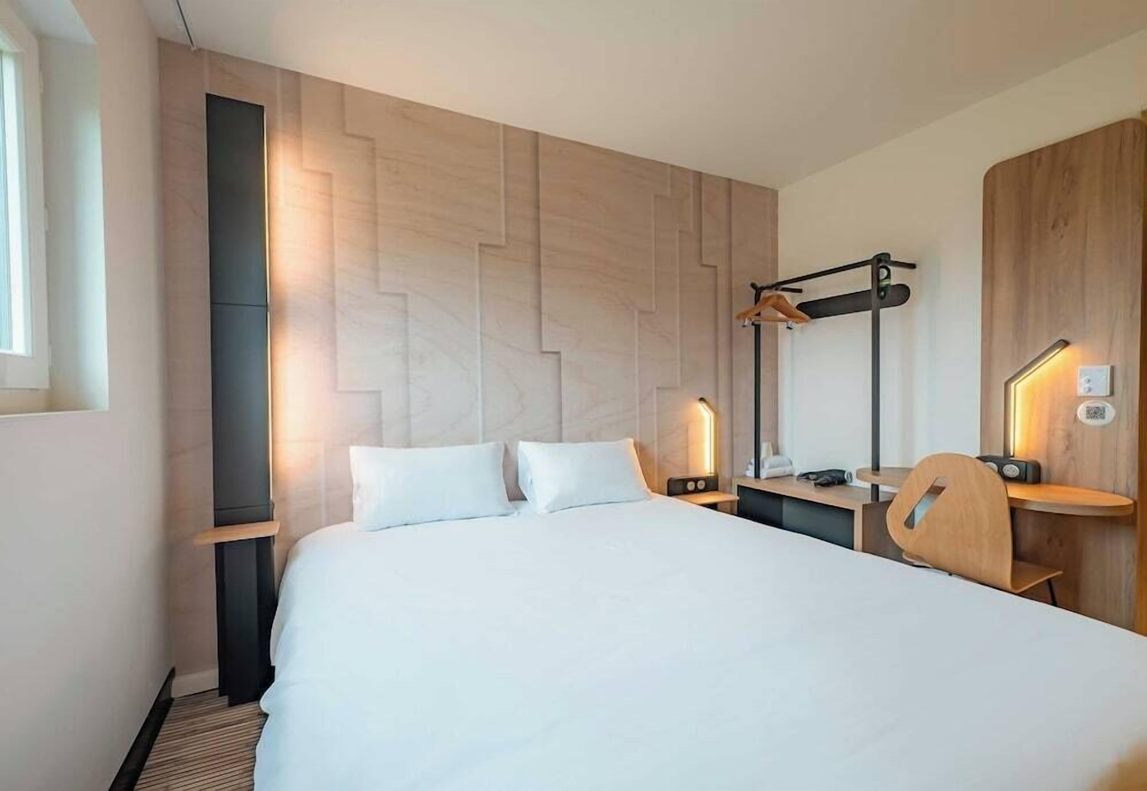 Quarto de hotel com cama, mesas de cabeceira, escrivaninha, cadeira e guarda-roupa.