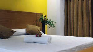 Uma cama bem arrumada com lençóis brancos, duas almofadas e uma toalha enrolada com uma flor.
