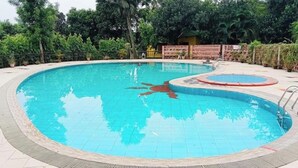 Piscina com deck ladrilhado, um pequeno ofurô e vegetação ao redor.