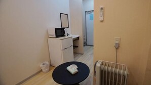 Quarto de hotel compacto com cozinha compacta, uma pequena mesa com lenços de papel, radiador branco e lixeira.