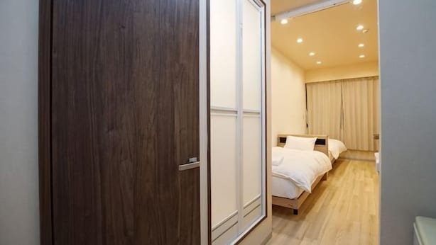 Quarto com guarda-roupa de madeira, cama com roupa de cama branca e luminária no teto.