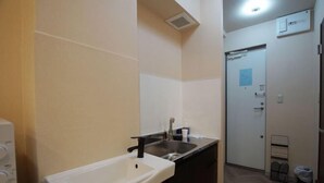 Casa de banho com lavatório branco, espelho e sanita. Há um pequeno contentor de lixo e um sapateiro perto da porta.