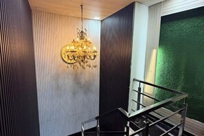 Uma escadaria com corrimão de vidro que leva a um patamar, um candelabro e uma parede verde com textura.