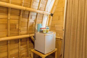Quarto com paredes de bambu e um pequeno eletrodoméstico branco sobre um suporte de madeira.