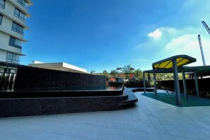 Um pátio com uma fonte, área de estar coberta e um edifício com vários andares.