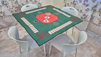 Mesa com toalha verde e padrões vermelhos e brancos, rodeada por cadeiras brancas.