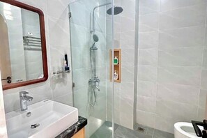 Casa de banho com chuveiro em cabine de vidro, pia branca e espelho com moldura de madeira.
