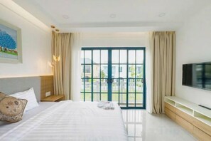 Quarto de hotel com cama, televisão, janela com cortinas e um quadro na parede.
