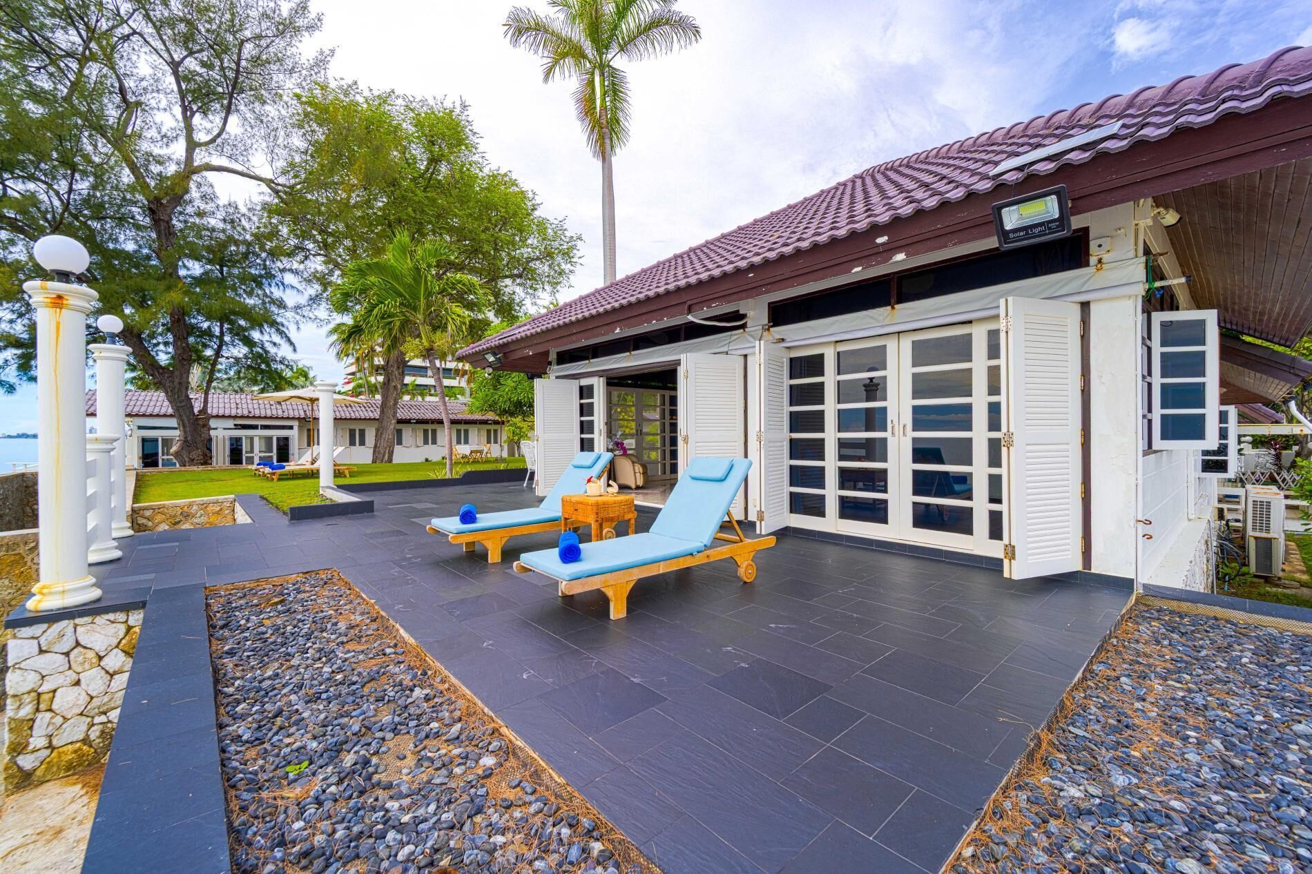 Resort com área externa coberta, com duas espreguiçadeiras e uma mesa à beira da piscina.