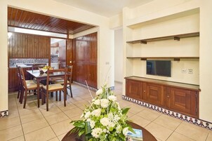 Uma sala de jantar com mesa e cadeiras de madeira, televisão fixada na parede e um vaso decorativo sobre uma mesa.