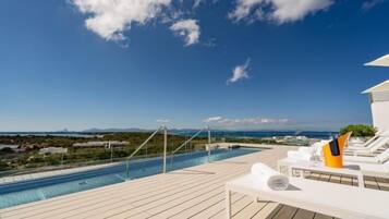 Área da piscina com espreguiçadeiras e vista para a paisagem.