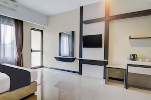 Quarto de hotel com cama, escrivaninha, televisão de tela plana, janela com cortinas e prateleira na parede.