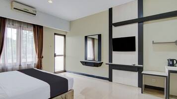Quarto de hotel com cama, televisão, espelho, mesa pequena e ar condicionado.