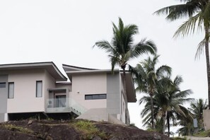 Um edifício moderno de dois andares com varanda, rodeado por palmeiras.