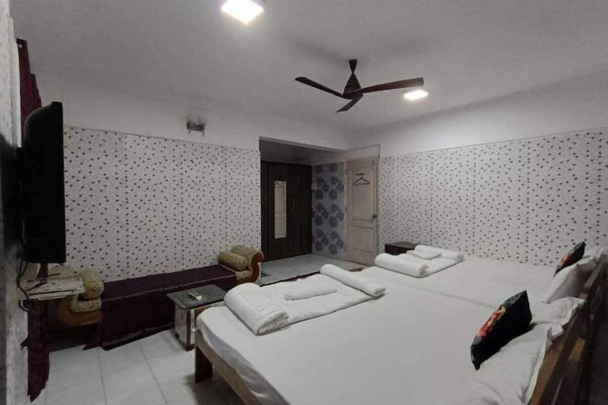 Quarto de hotel com duas camas, televisão, escrivaninha, cadeira e ventoinha no teto.