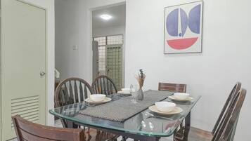 Uma sala de jantar com mesa de vidro, cadeiras de madeira e um quadro abstrato pendurado na parede.