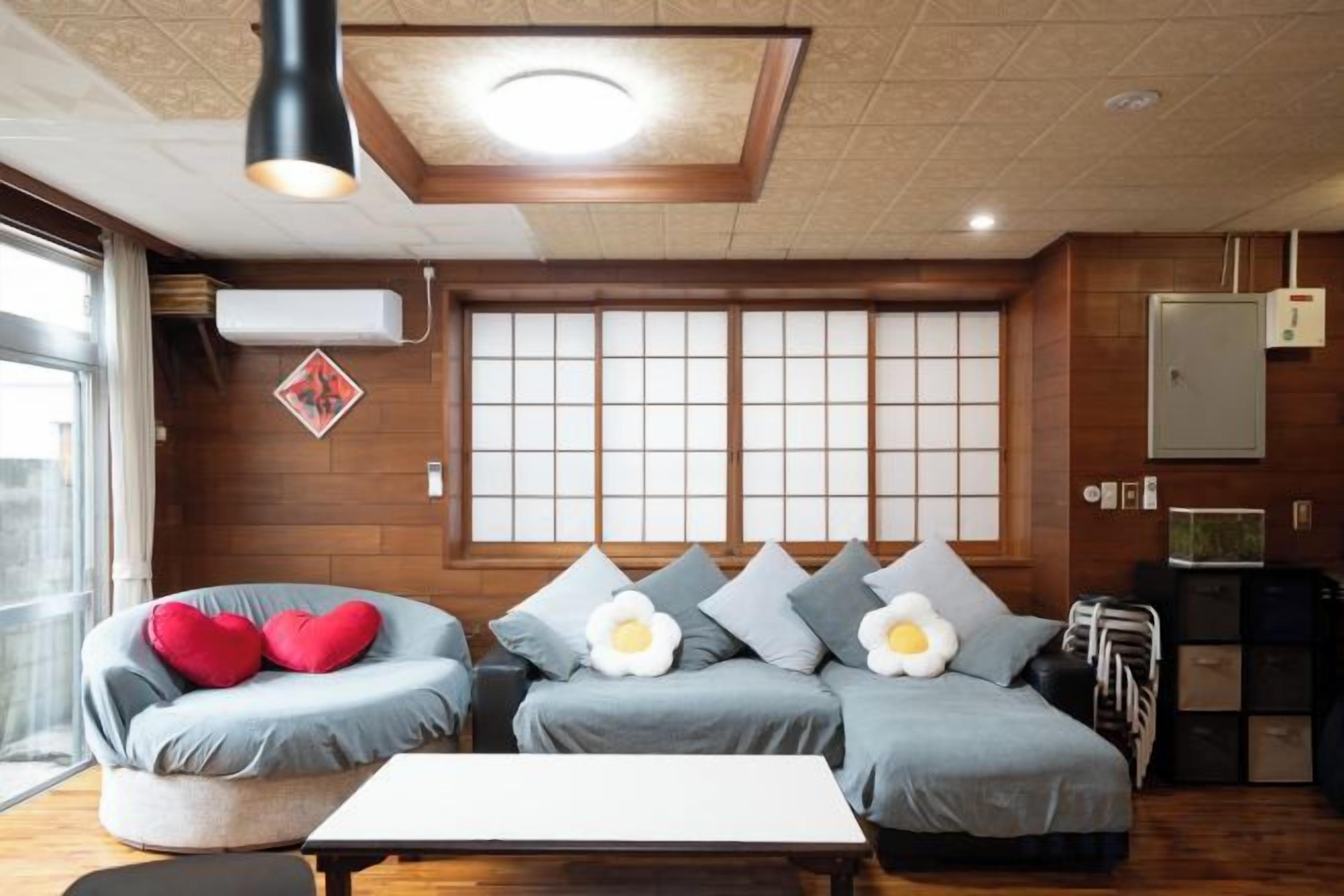 Um quarto com teto baixo, um sofá com almofadas, uma mesa e uma janela com vista.