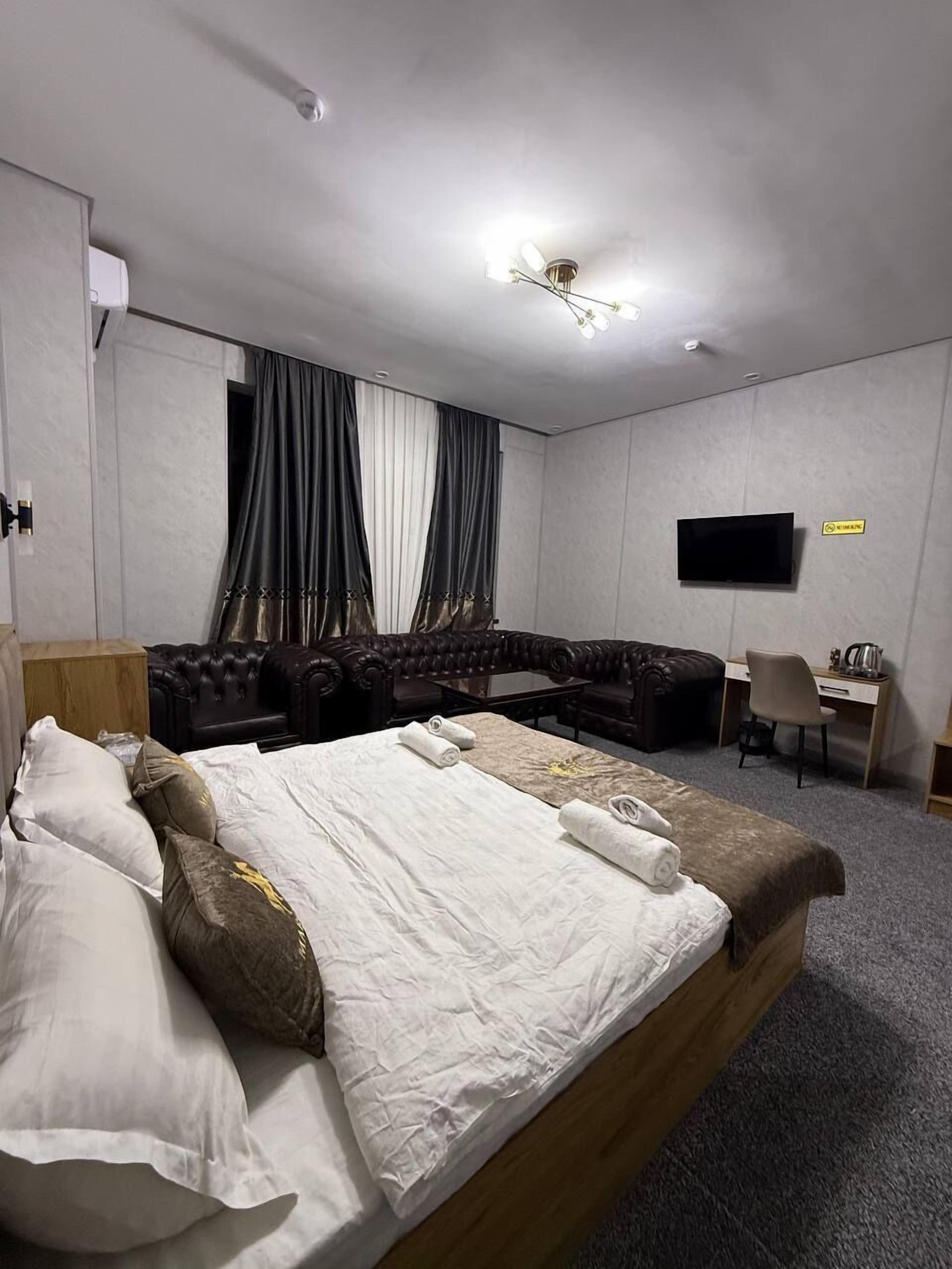 Quarto de hotel moderno com uma cama grande, um sofá-cama, uma escrivaninha e uma televisão de tela plana.