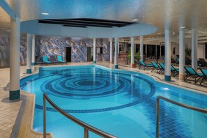 Uma piscina interior com design circular, rodeada por espreguiçadeiras e uma parede de mármore.