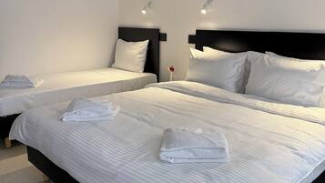 Quarto de hotel com duas camas, cada uma com lençóis e almofadas brancos, uma cama grande com uma toalha dobrada e duas pinturas emolduradas de animais nas paredes.