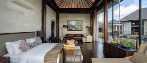 Um quarto espaçoso com uma cama grande, um espaço de estar com sofá e poltrona, e uma varanda com vista para a região.