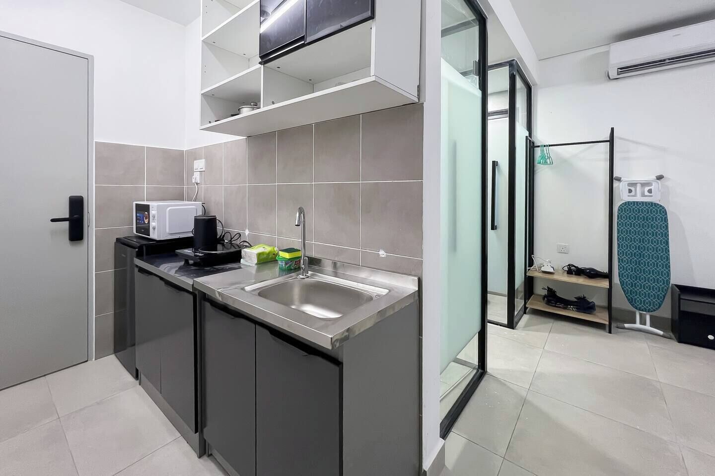 Cozinha moderna com micro-ondas embutido, pia e cafeteira. Porta de chuveiro em vidro e porta-toalhas suspenso.