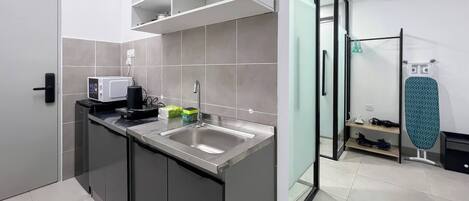 Cozinha moderna com micro-ondas embutido, pia e cafeteira. Porta de chuveiro em vidro e porta-toalhas suspenso.