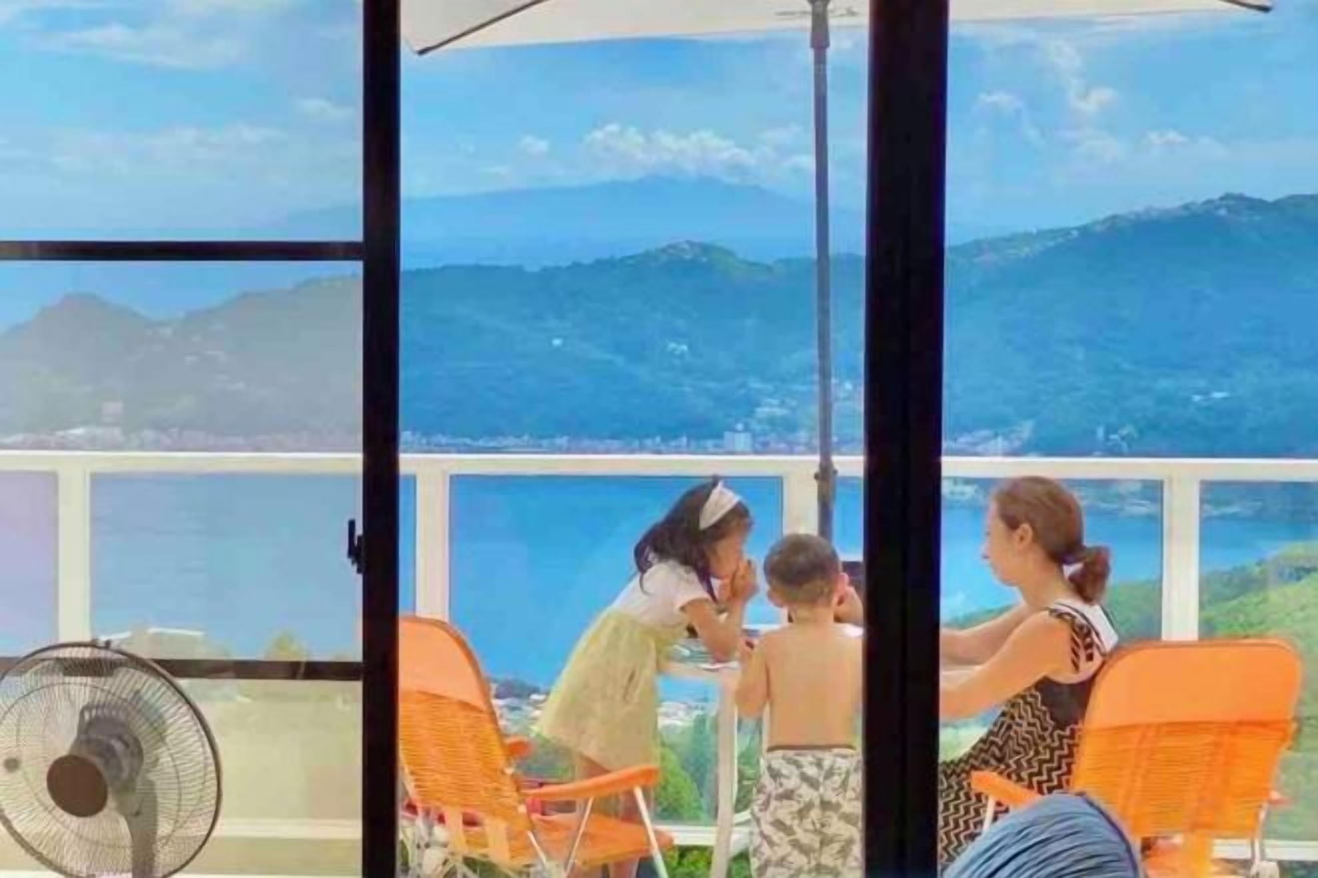 Varanda com mesa e cadeiras, com vista para uma paisagem montanhosa e um corpo de água.